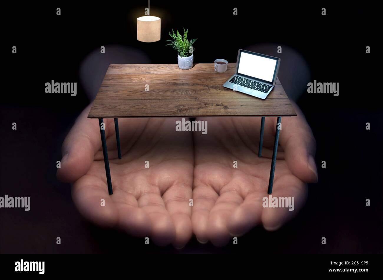 Hands outstretched holding a miniature office desk with laptop and lamp ...