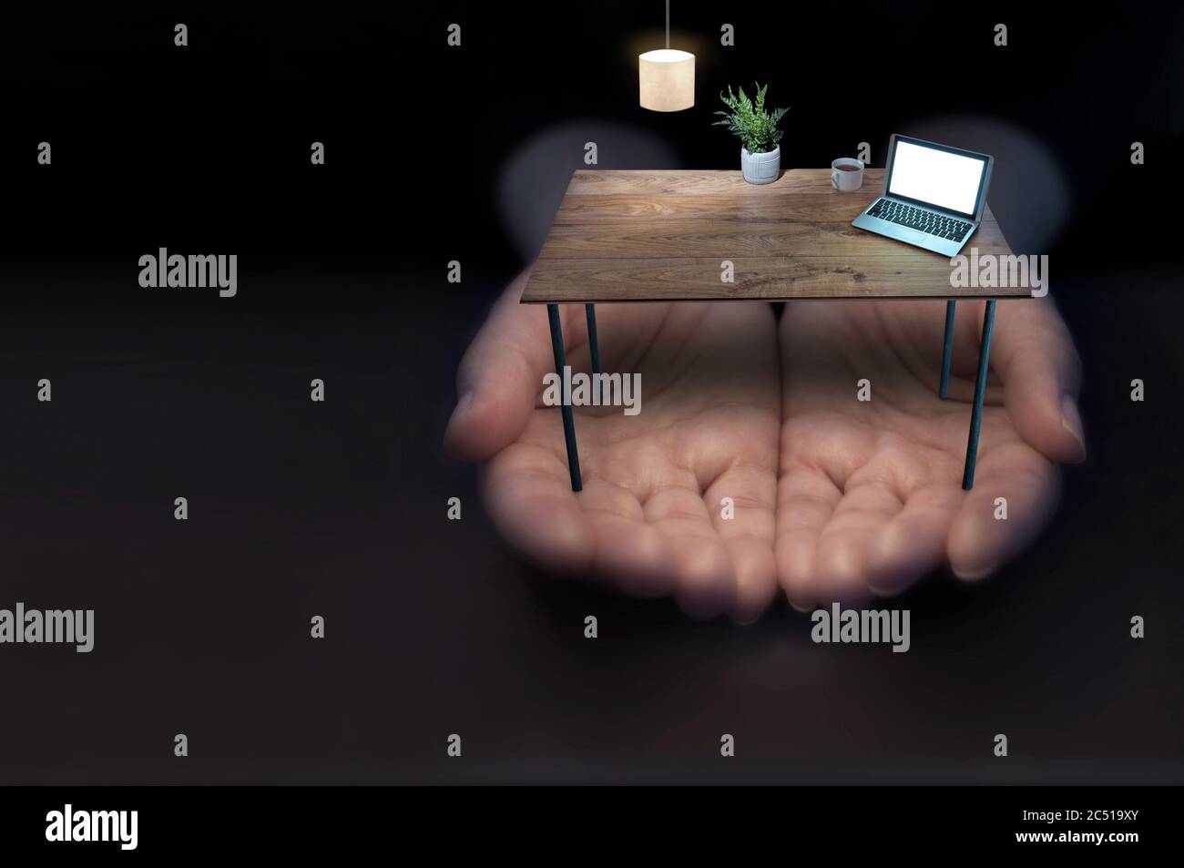 Hands outstretched holding a miniature office desk with laptop and lamp ...