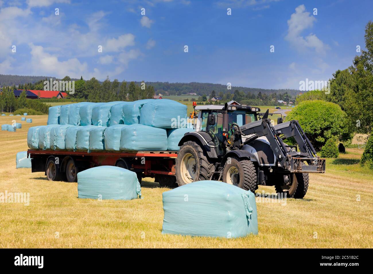 Farmer drives Valtra tractor in front of agricultural trailer full of ...