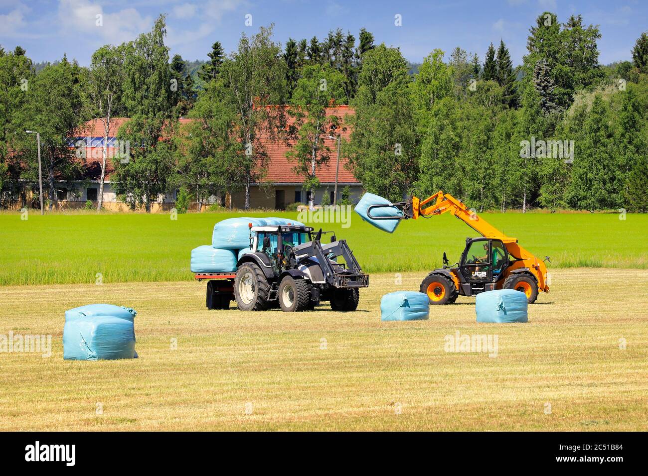 Rural scene with hay field and JCB reach forklift stacking silage bales ...