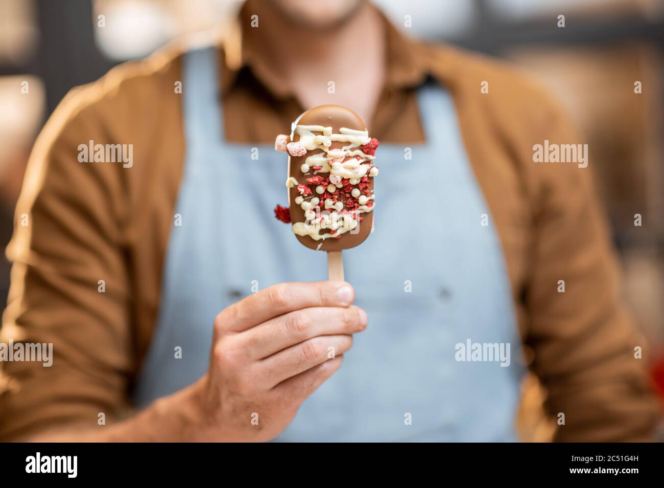 Salesman holding chocolate ice cream on a stick, selling ice creams at ...