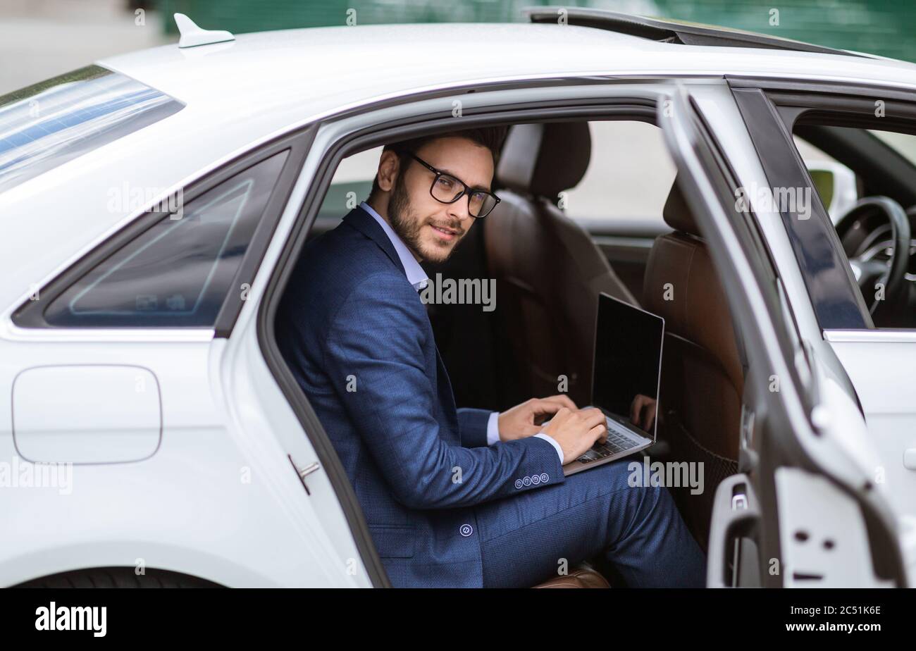 Handsome businessman working with laptop computer sitting at back seat ...