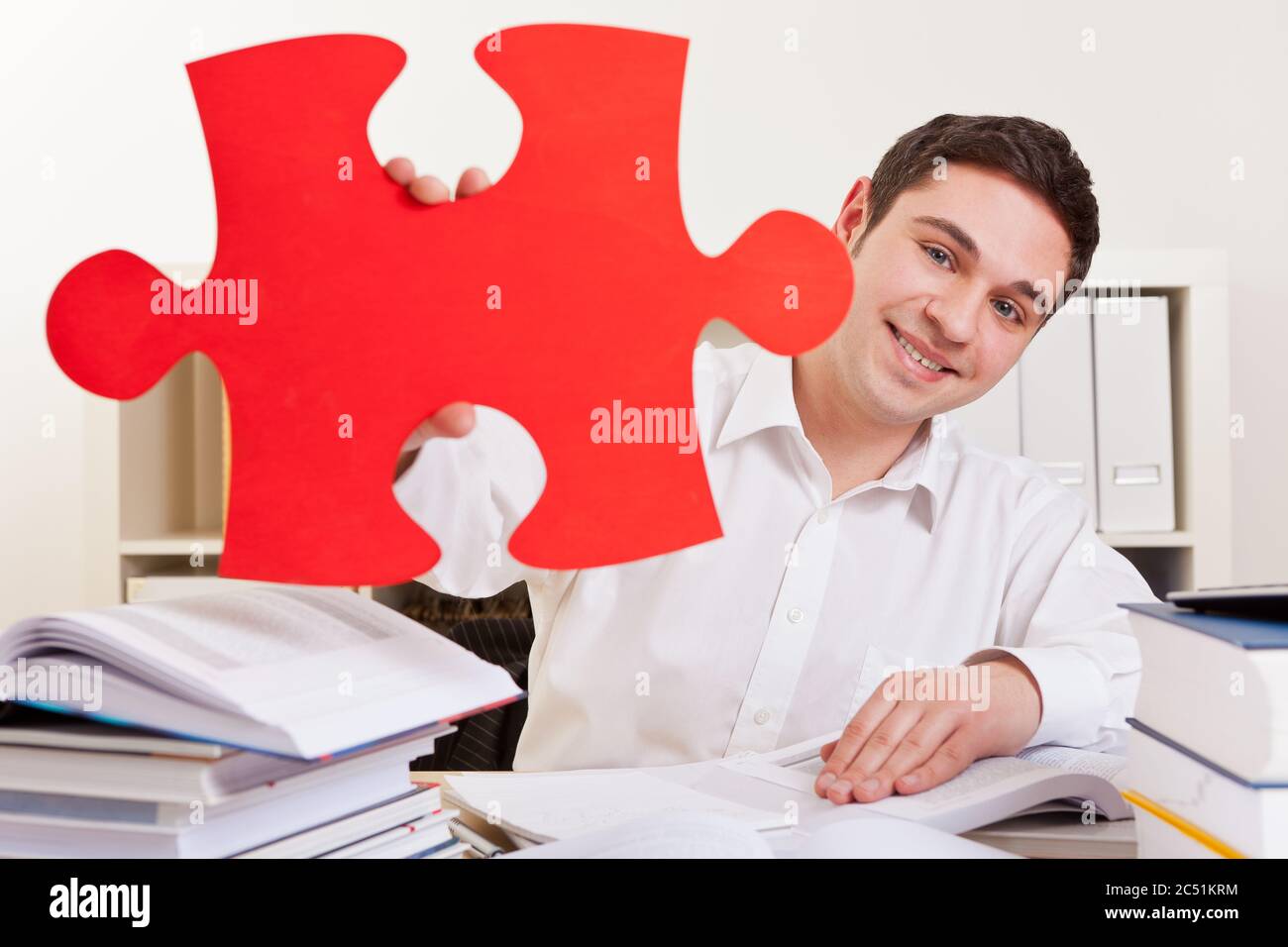 Laughing student at the desk is holding a large red puzzle piece Stock ...