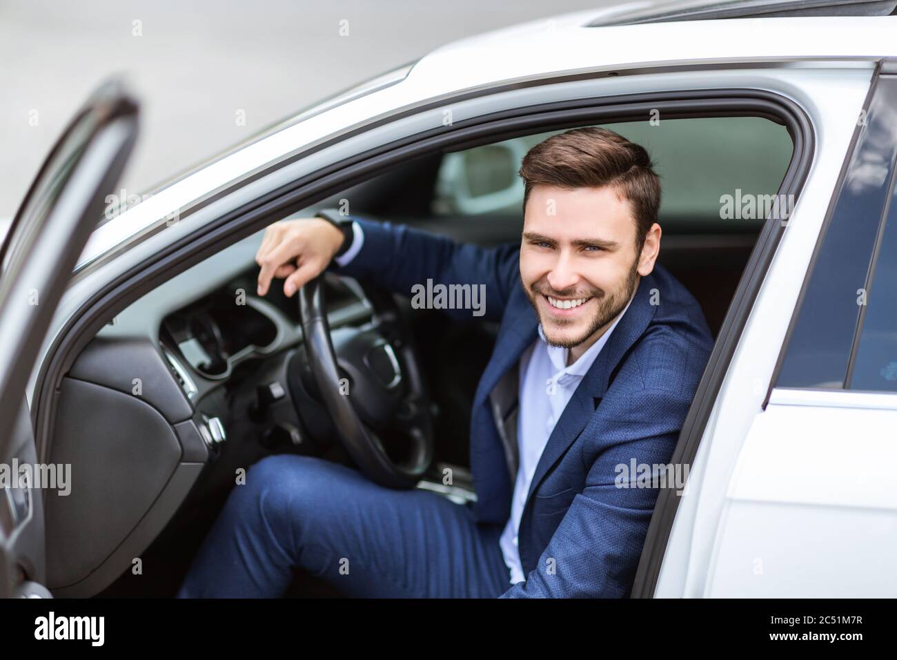Portrait of smiling corporate employee sitting on driver's seat of his ...