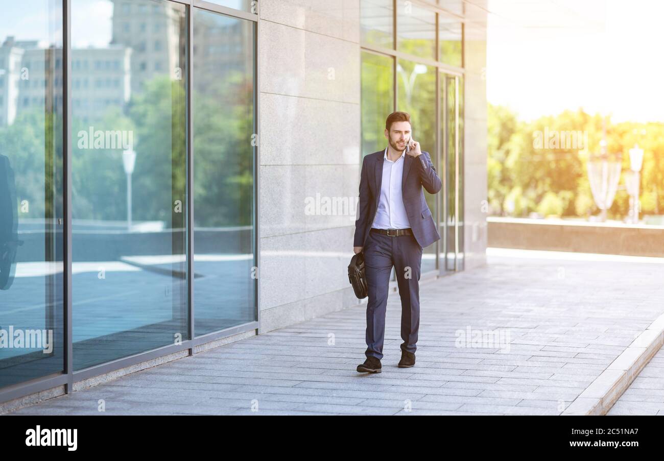 Corporate employee talking on mobile phone while walking near office ...