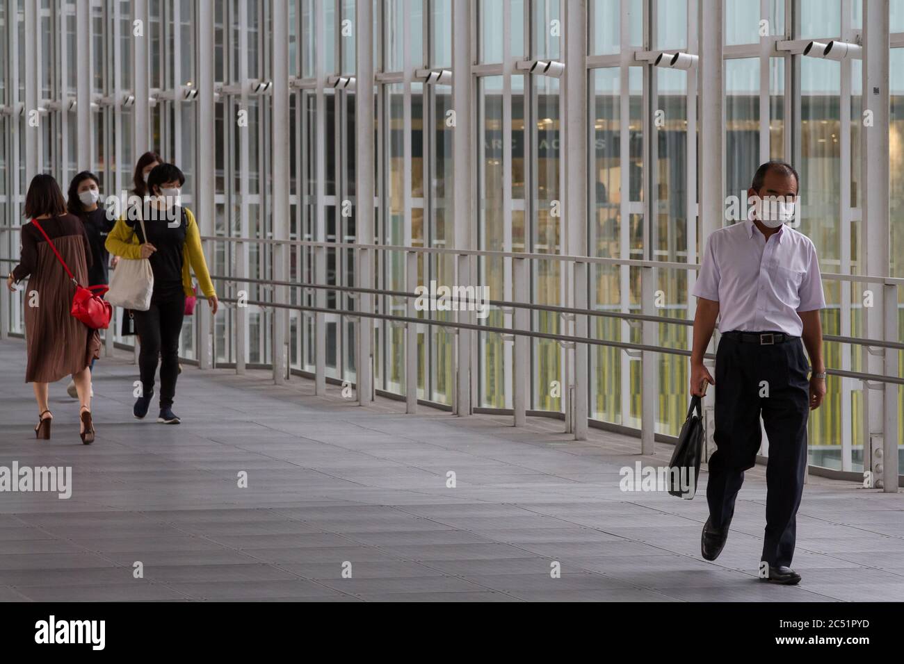 A Japanese salaryman and women, wearing face masks, walking a covered ...