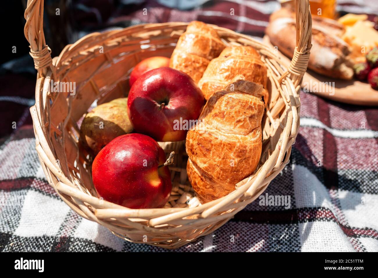 Picnic bread, croissant basket with fruit on cloth with bright sunlight ...