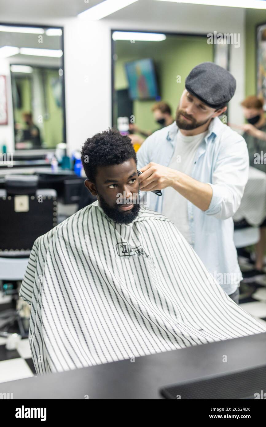 Happy young black man being trimmed with electric clipper machine in ...