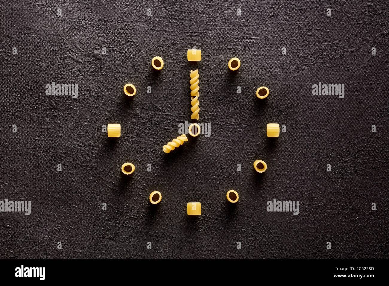 Uncooked pasta designed in clock shape on dark brown background. Eating ...