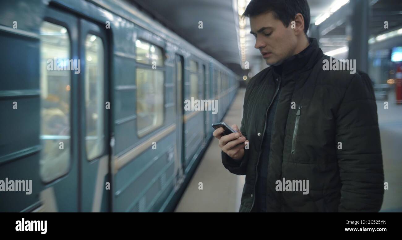 Young man using smart phone to type text message at the underground ...