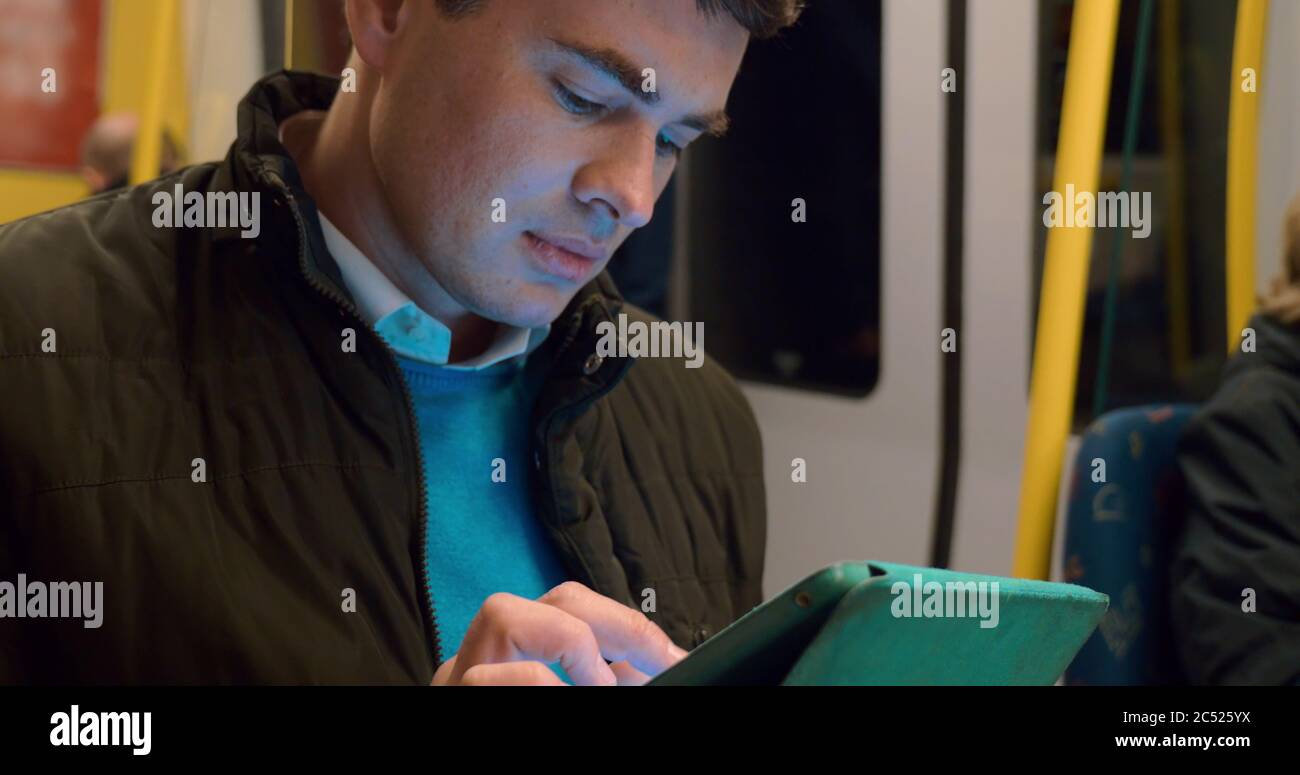 Young man using tablet computer in underground train. Entertaining with ...