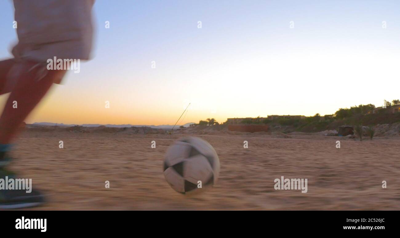 Steadicam shot of a person playing football on a sand field. He's ...
