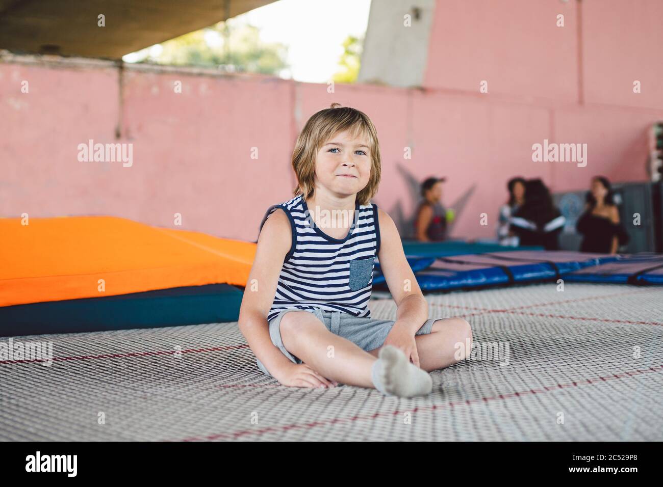 gymnast sitting on trampoline in fitness center. Tired child sits on ...