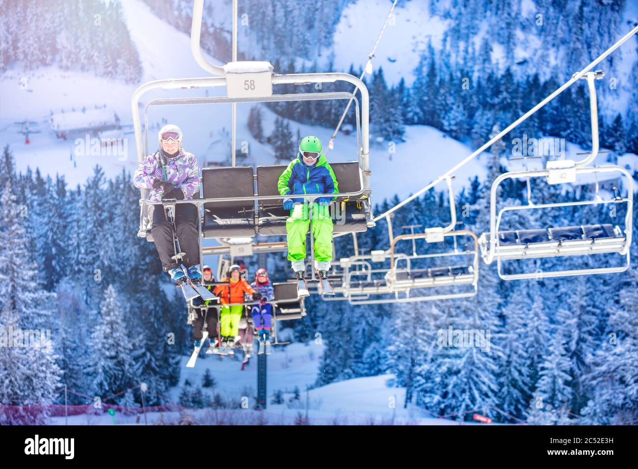 Boy and girl sit on chairlift with friends going on second chair all ...