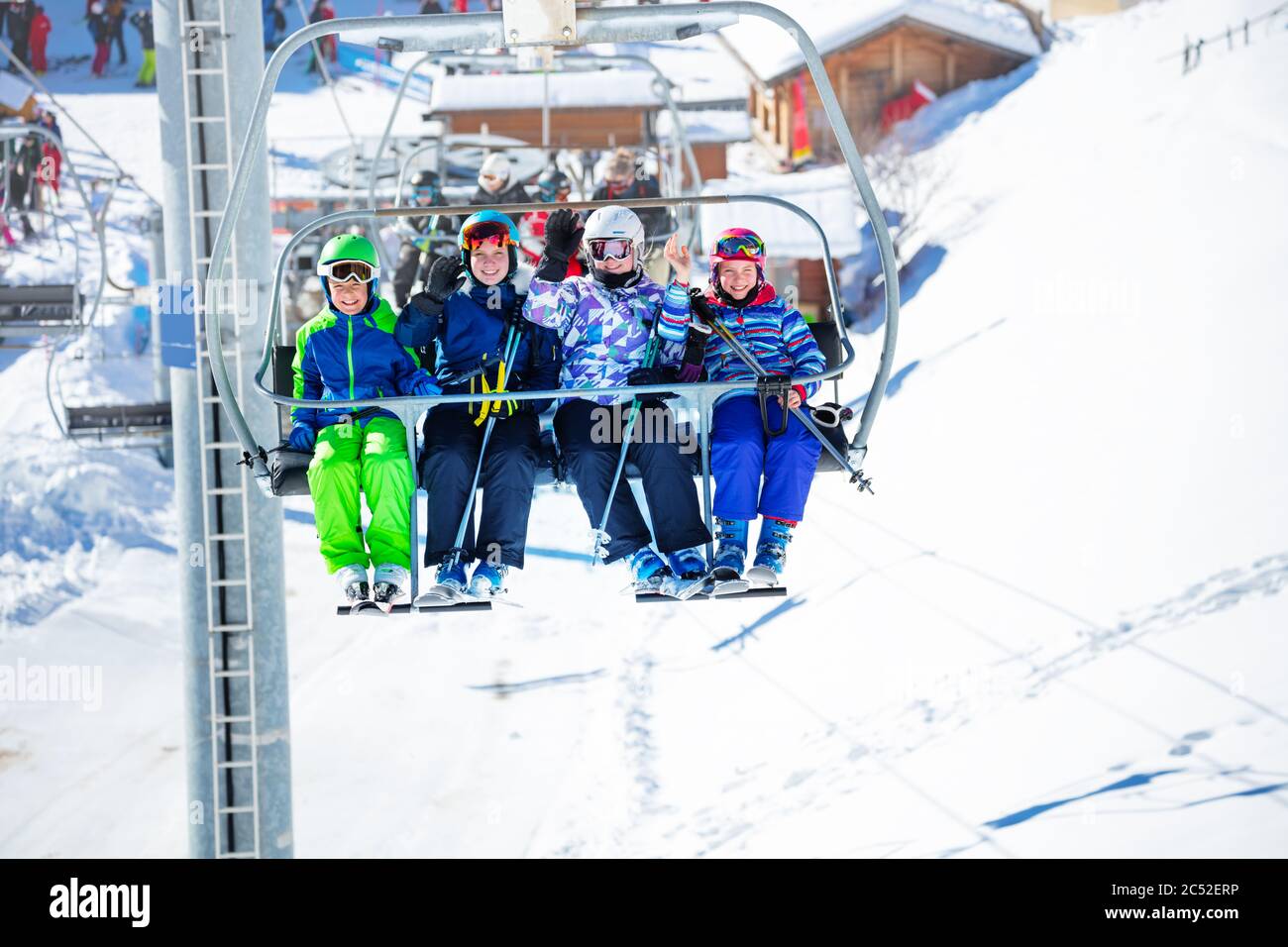 Group of skiers children sit on chairlift and wave hands going on the ...