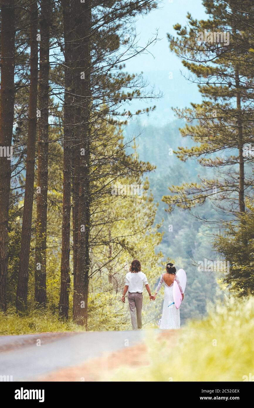 Vertical shot of a just married couple in a forest with a surfboard ...