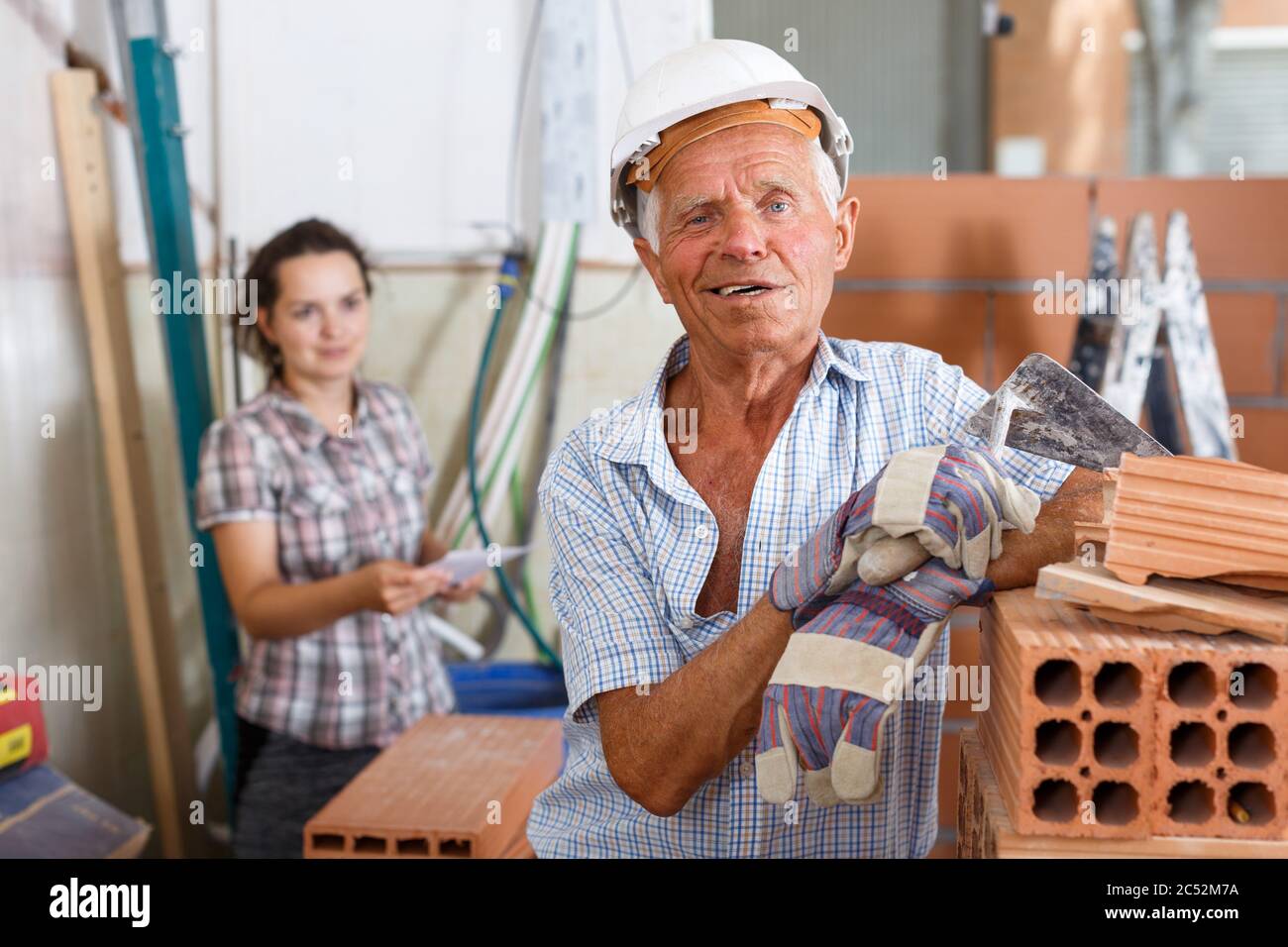 Happy experienced elderly bricklayer posing near red brick stack in ...