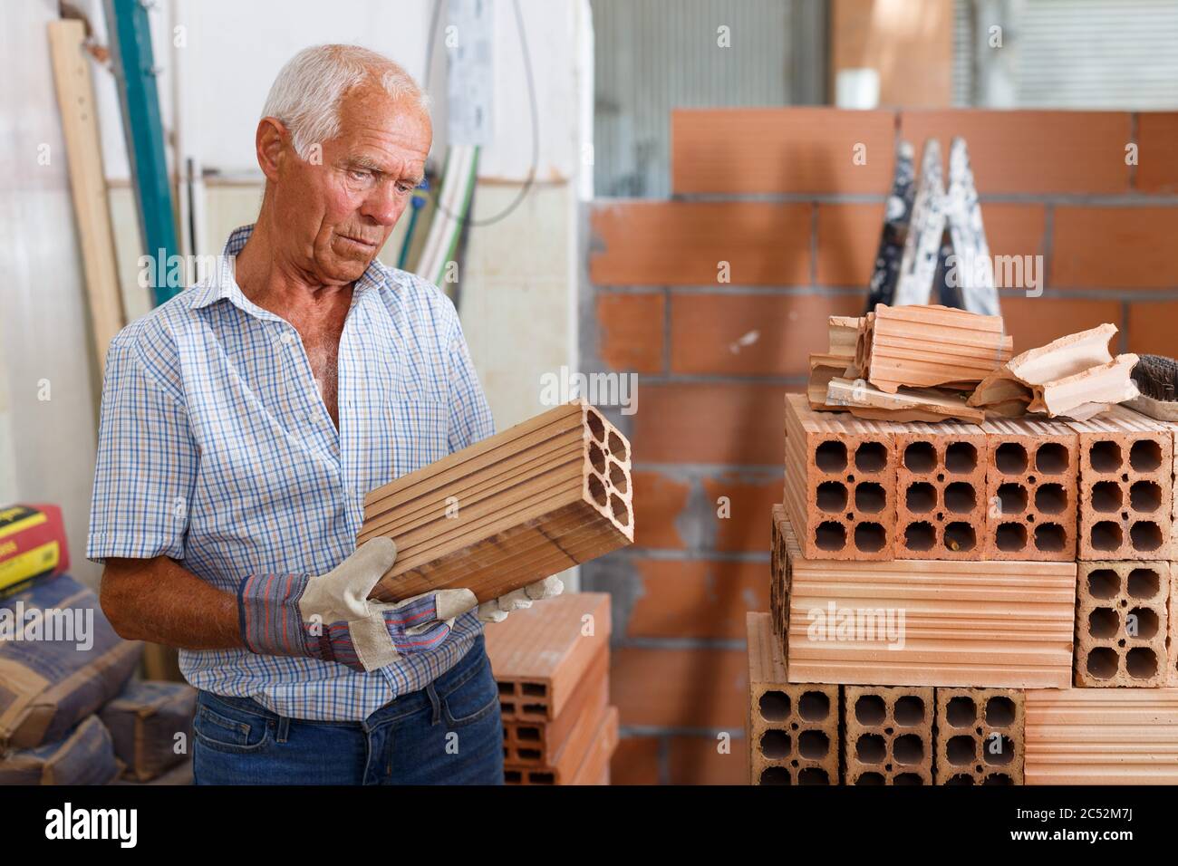Skillful older man inspecting brick for installing wall in building ...