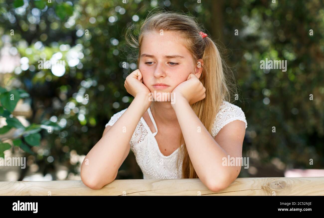 Portrait of upset teenage girl standing near fence in green park at ...