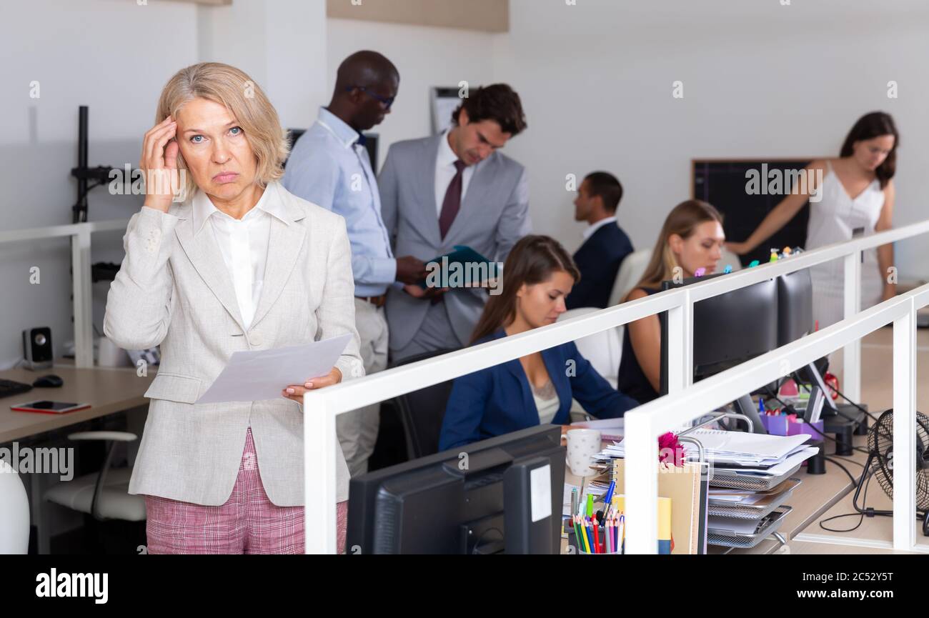 Confused mature woman office worker holding papers in office among ...