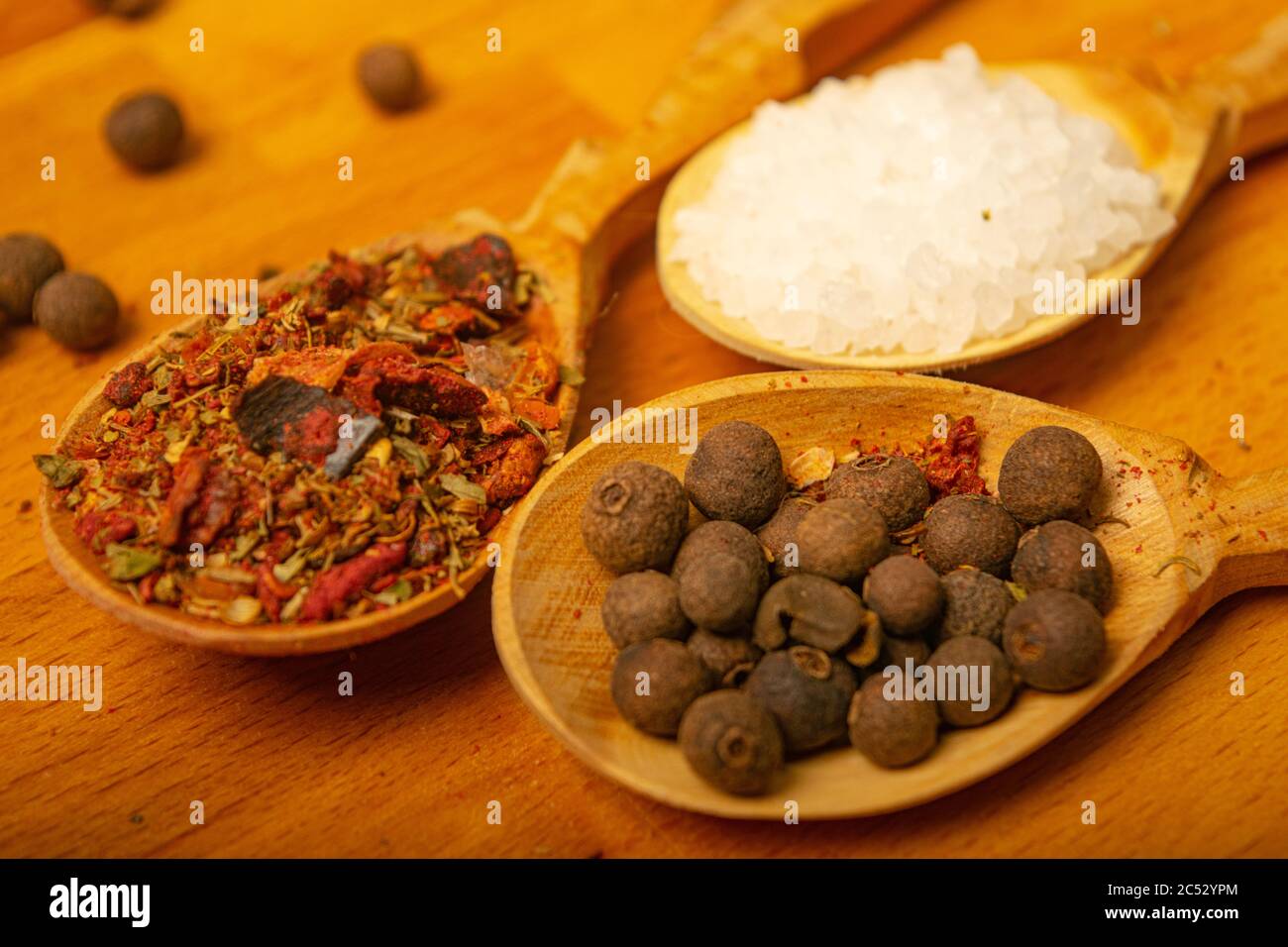 Black allspice, coarse salt and various ground spices in wooden spoons ...