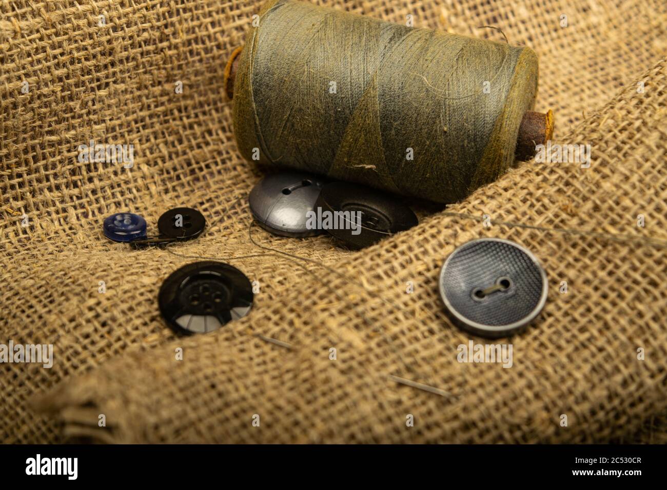 Different buttons and a spool of thread on the burlap with a rough ...