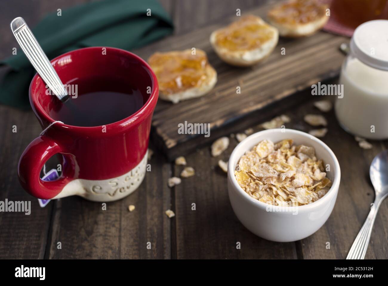 Breakfast table with a bowl of cereal, a cup of tea and some buns with ...