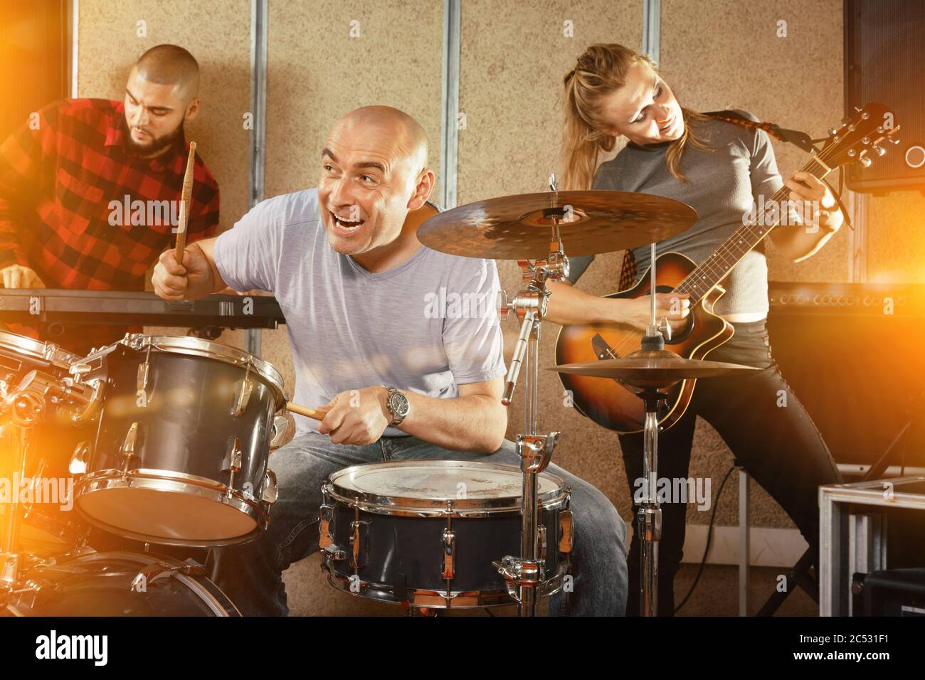 Expressive smiling glad drummer with his bandmates practicing in ...