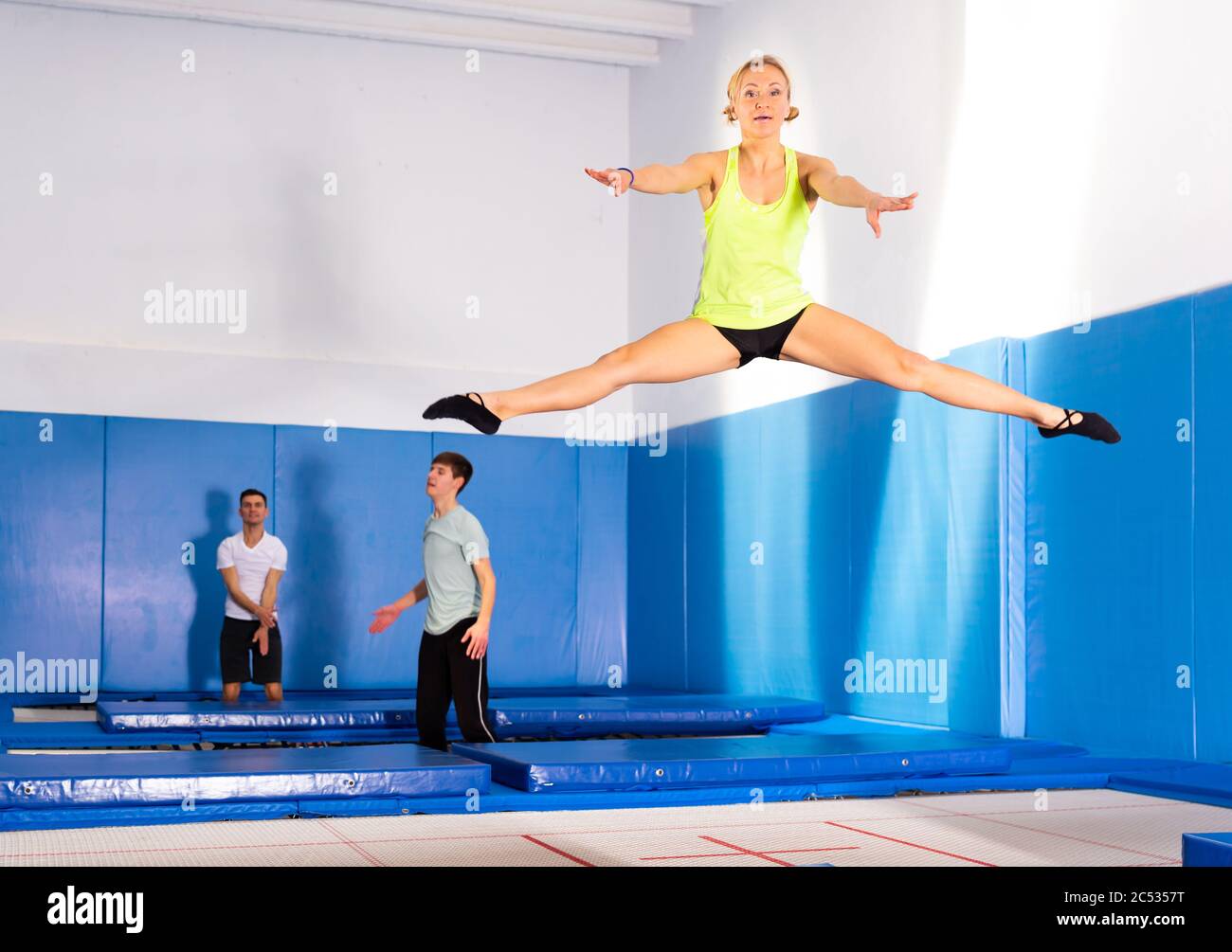 Athletic young woman training jumping movements in indoor trampolines ...