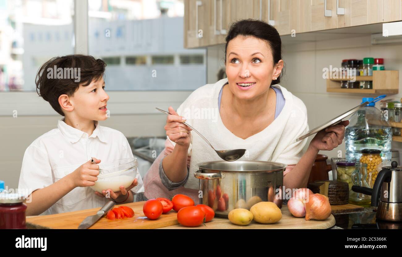 Smiling teen boy with his mother preparing family dinner together at ...