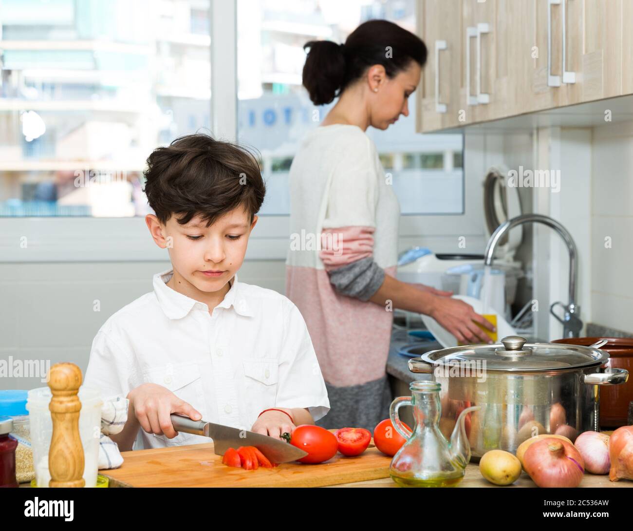 Smiling teen boy helping his mother to prepare family dinner at home ...