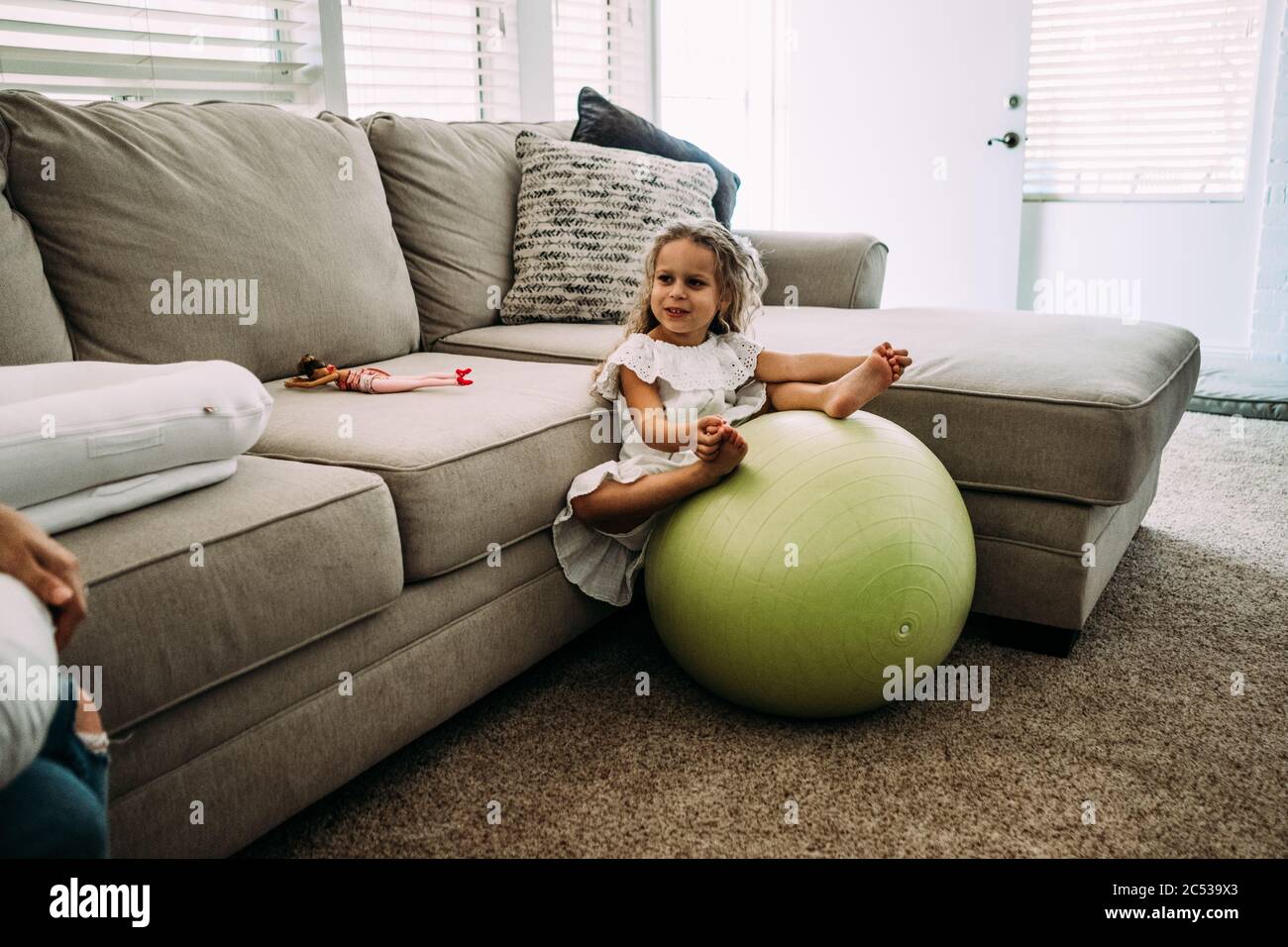 young girl sitting on a large ball in living room looking at someone ...