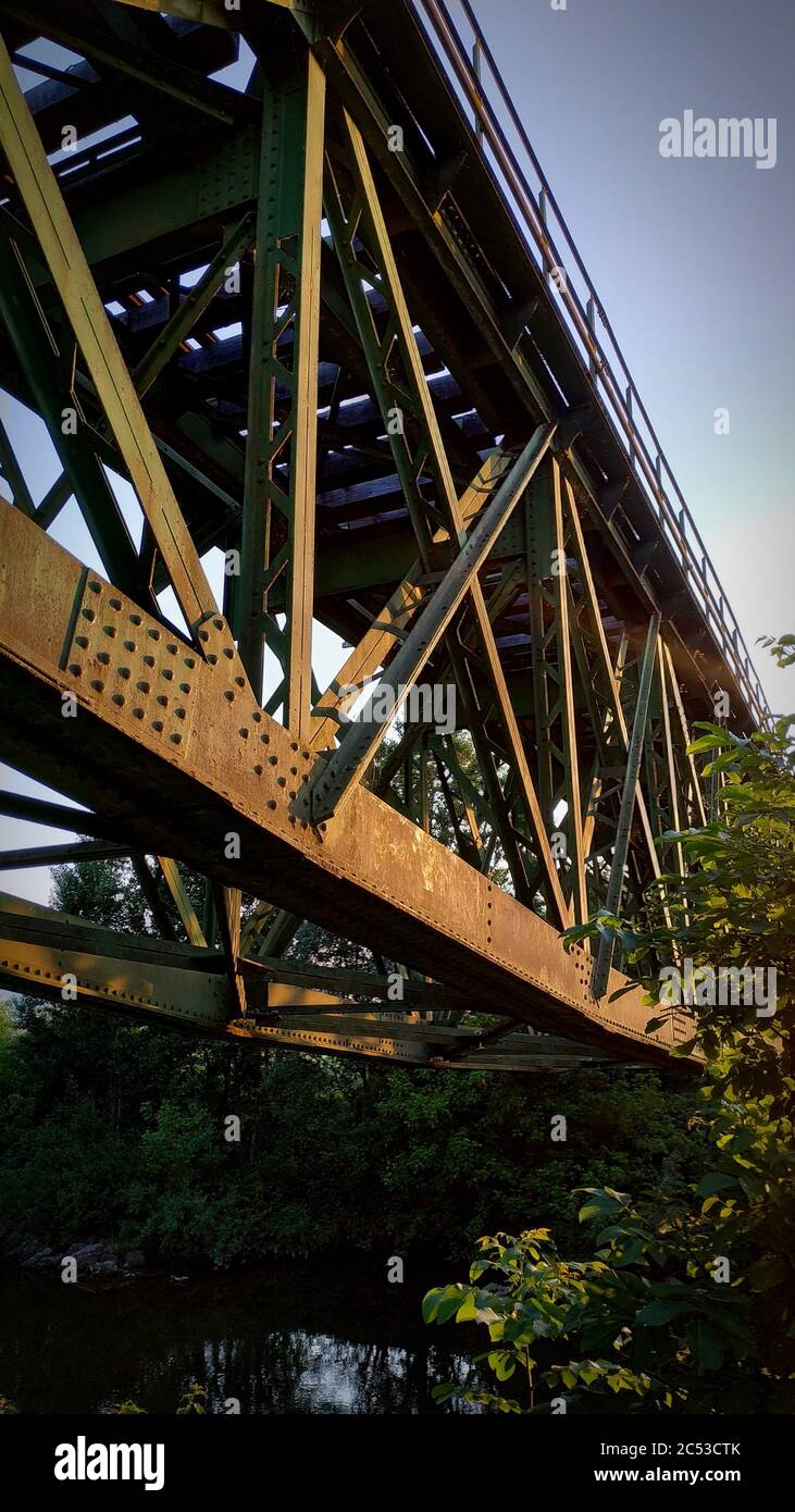 Vertical closeup shot of a rusted steel railroad bridge with some trees ...