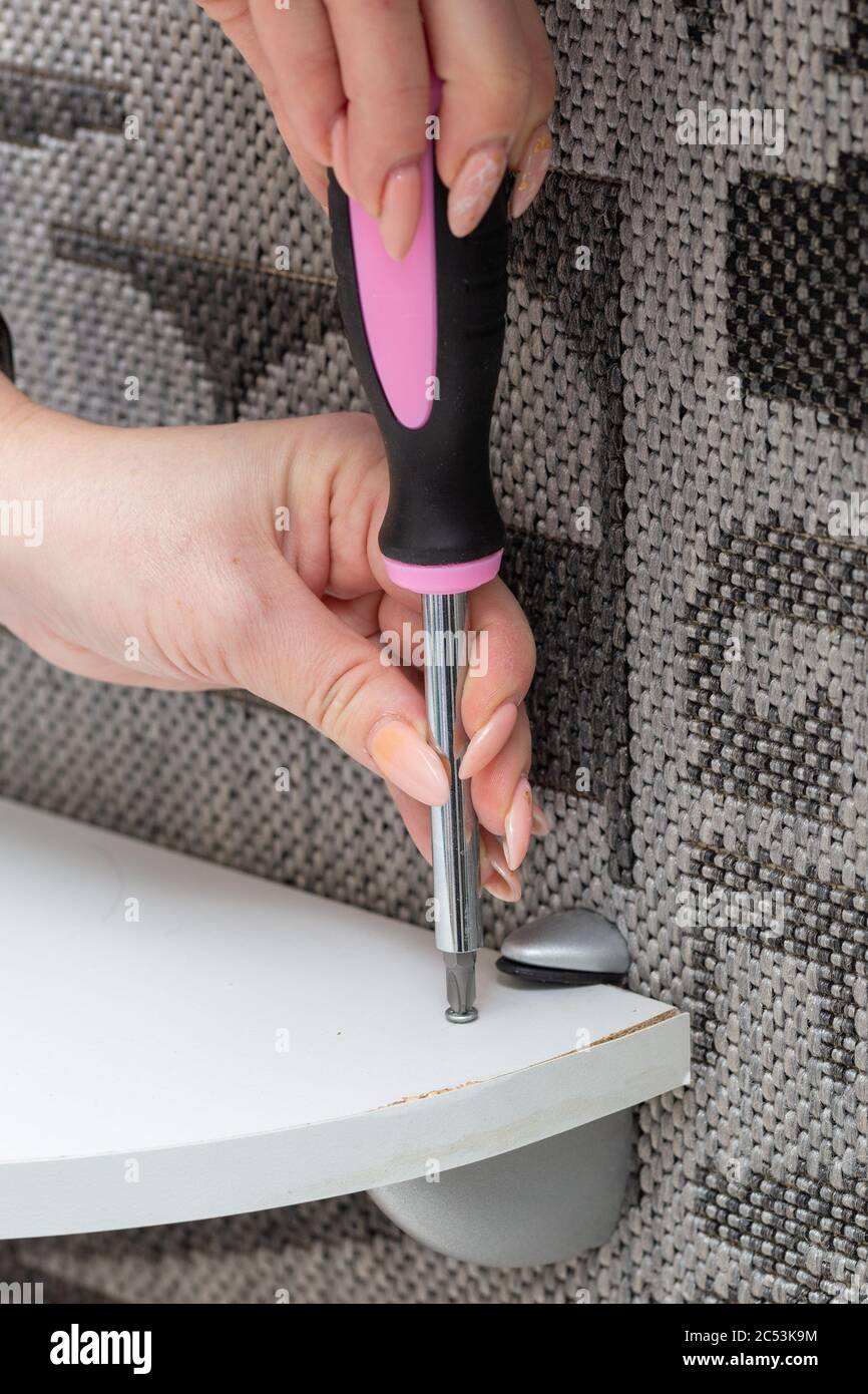 Women's hands hold a screwdriver and twist the screw on the shelf in ...