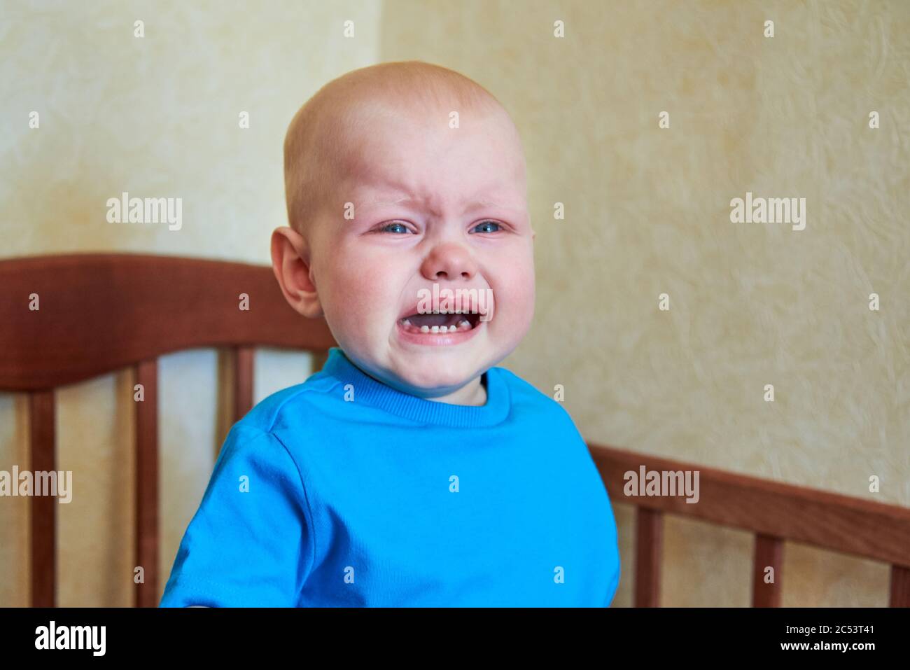 A little boy is standing in the crib, crying and calling his mother ...
