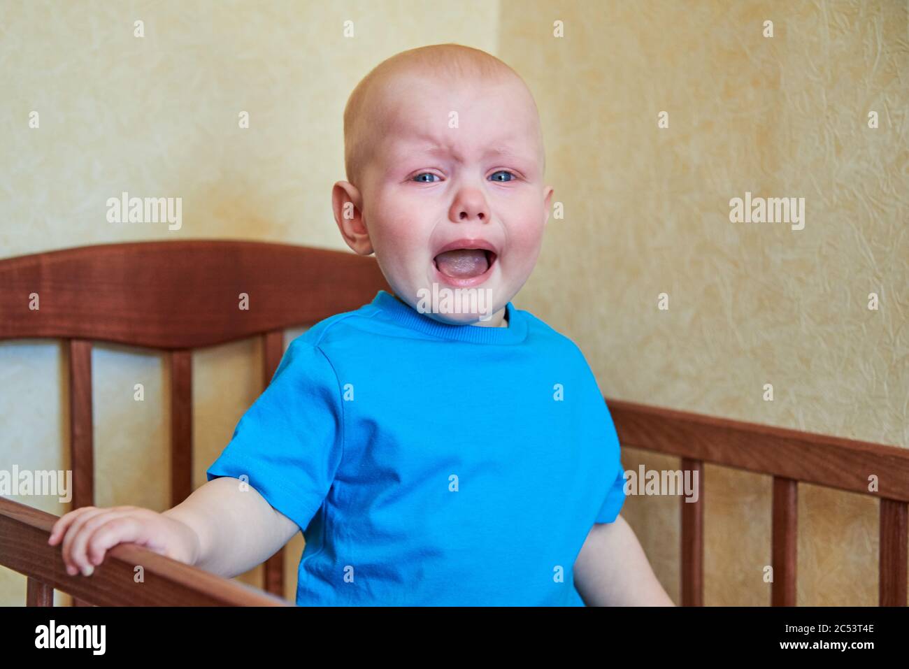 A little boy is standing in the crib, crying and calling his mother ...