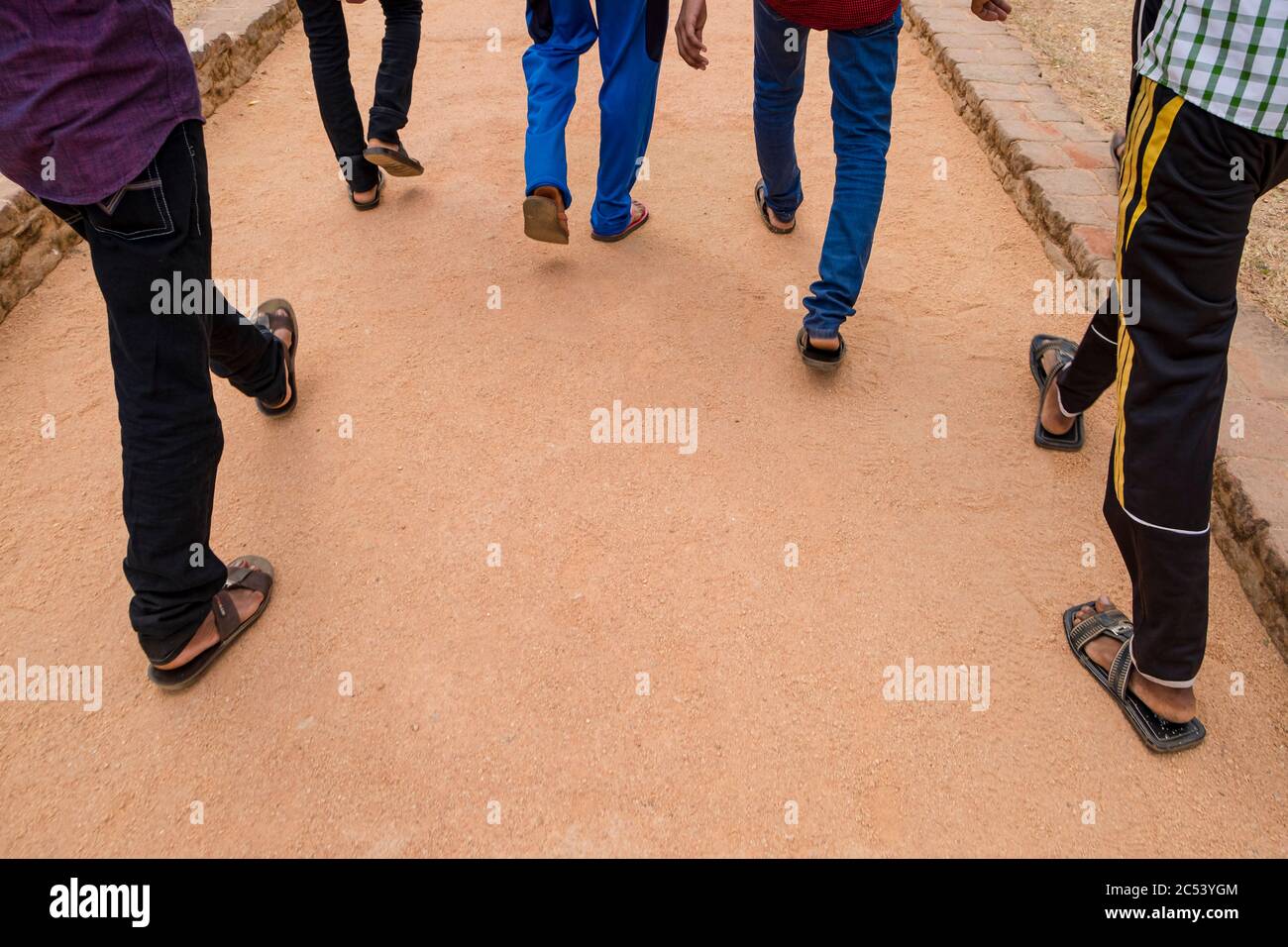 The legs of five men walking in sandals on a sandy path, Sri Lanka ...