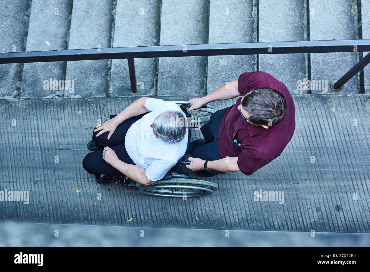 Middle-aged man pushes elderly lady in a wheelchair next to stairs ...