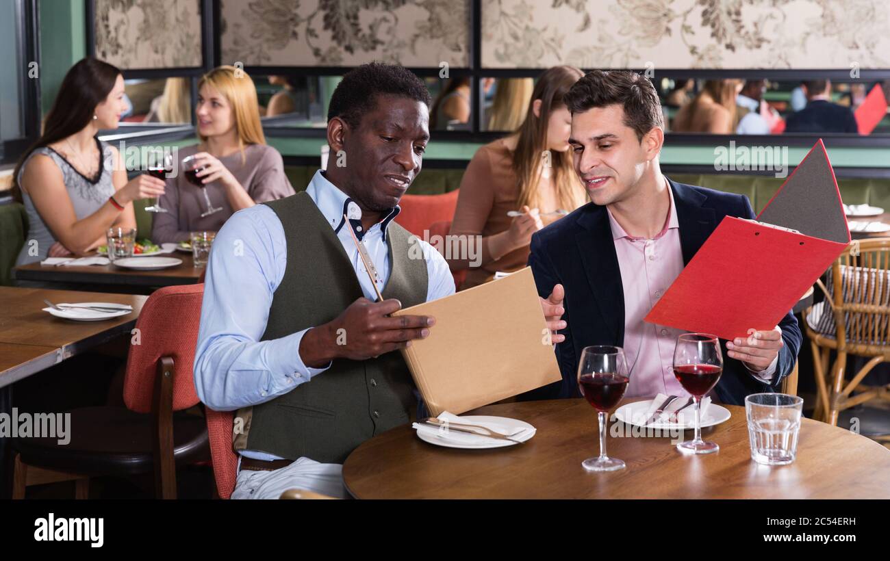 Happy smiling male friends choosing dishes from menu card in restaurant ...