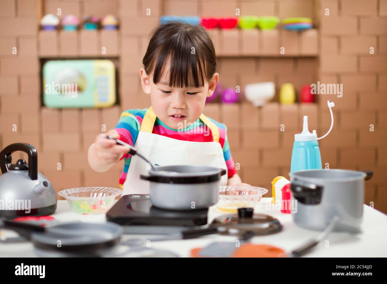 toddler girl pretend play food preparing role against cardboard blocks ...