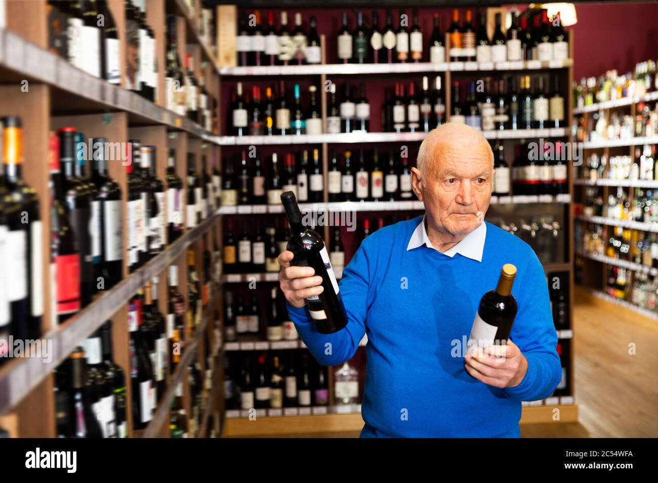 Serious man chooses red wine in a liquor store Stock Photo - Alamy