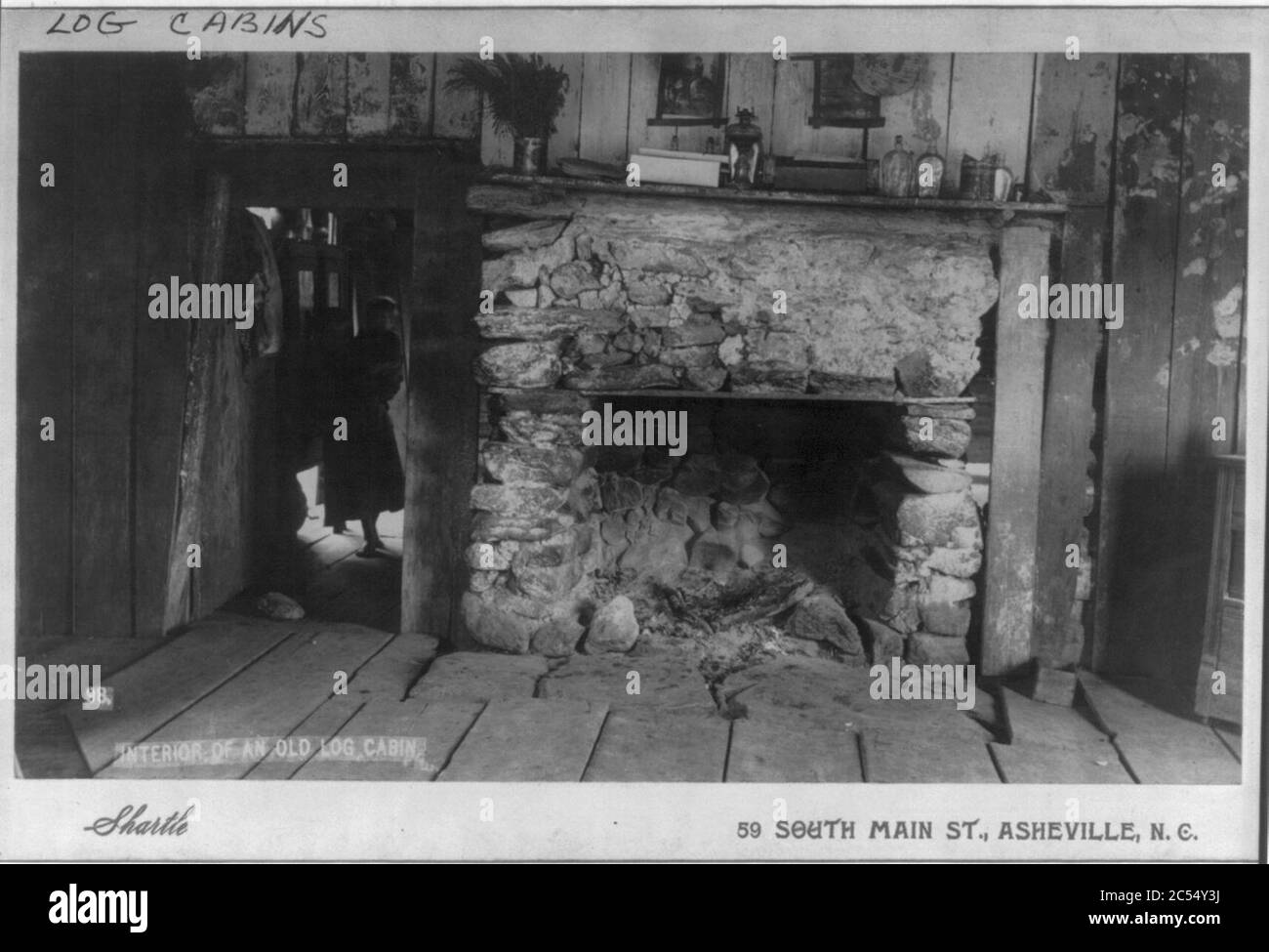 Interior of an old log cabin, shows fireplace and a child holding a ...