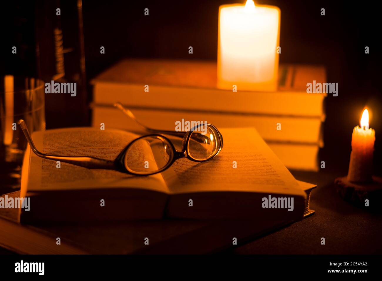 Glasses on the open book under the burning candle lights Stock Photo ...