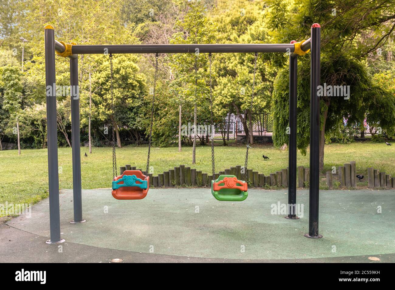 double swing stands empty in a small green park, with colorful plastik ...