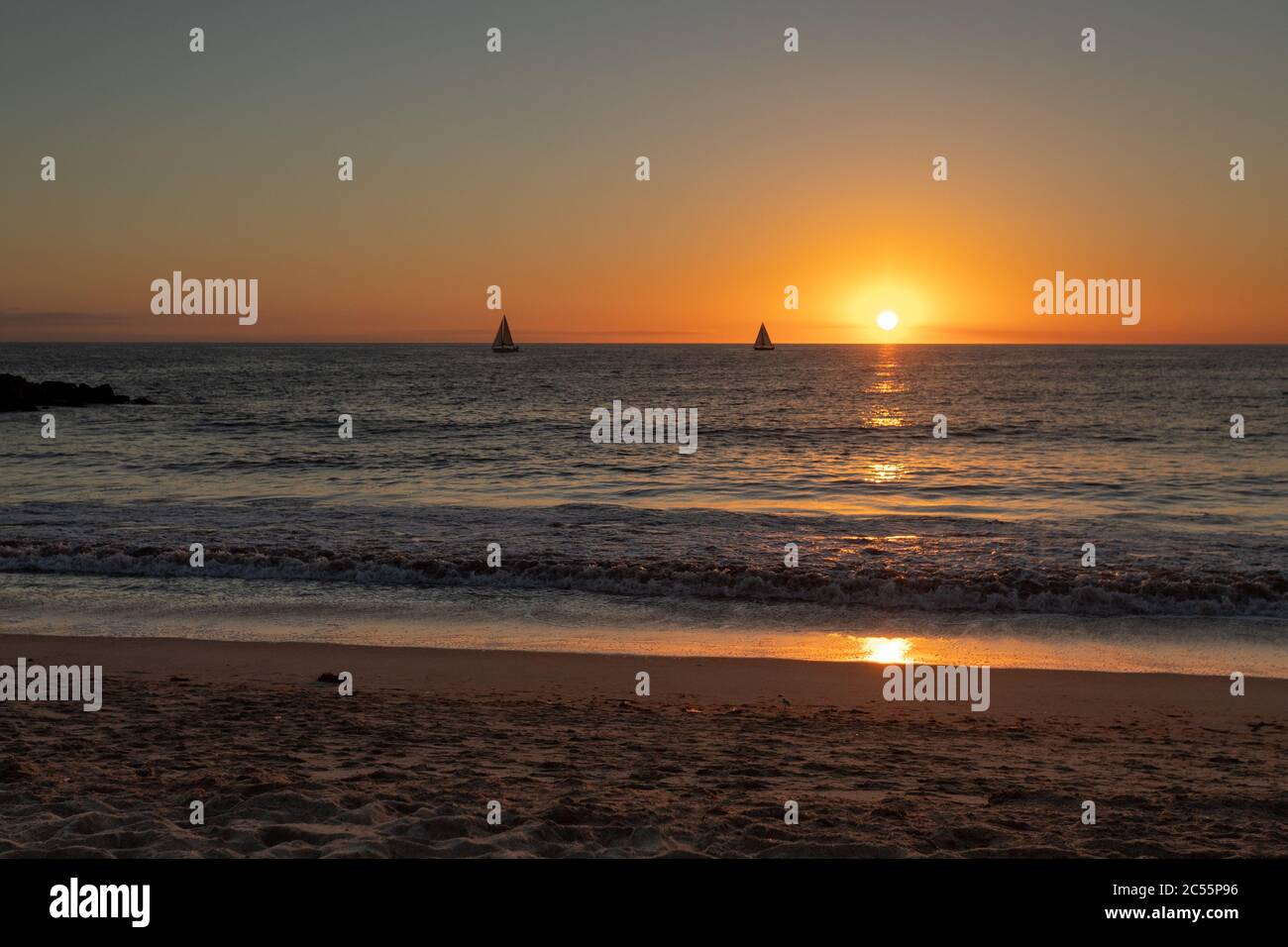 Sailboats sailing on the wavy ocean under the gleaming orange sunset ...