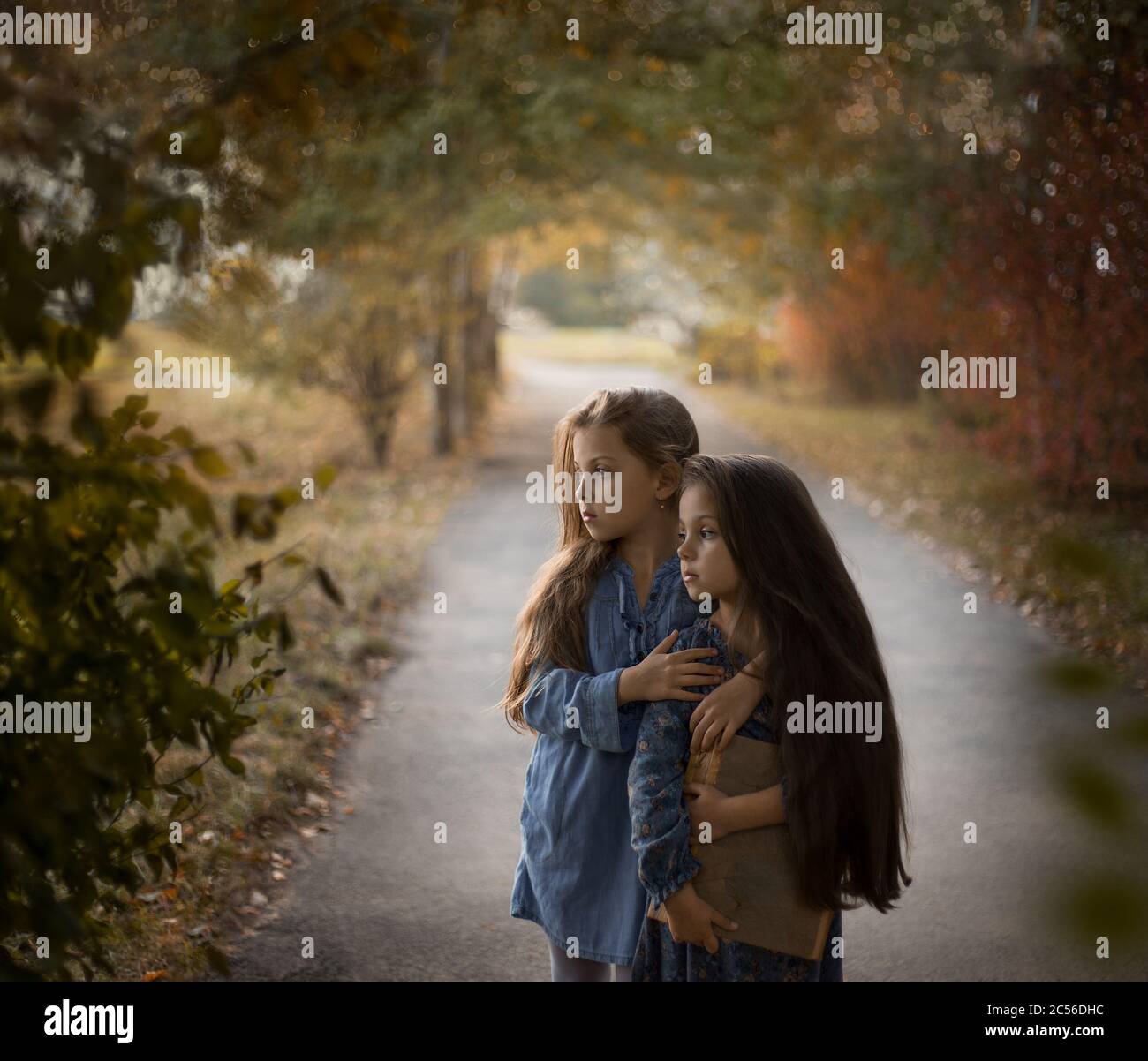Sisters with a family album in their hands stand in the fall in nature ...