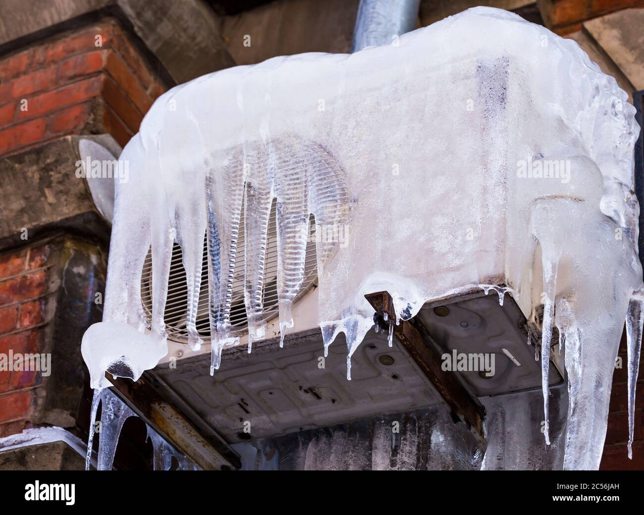 Air conditioner covered with ice and icicles. Aged old house wall. Cold ...