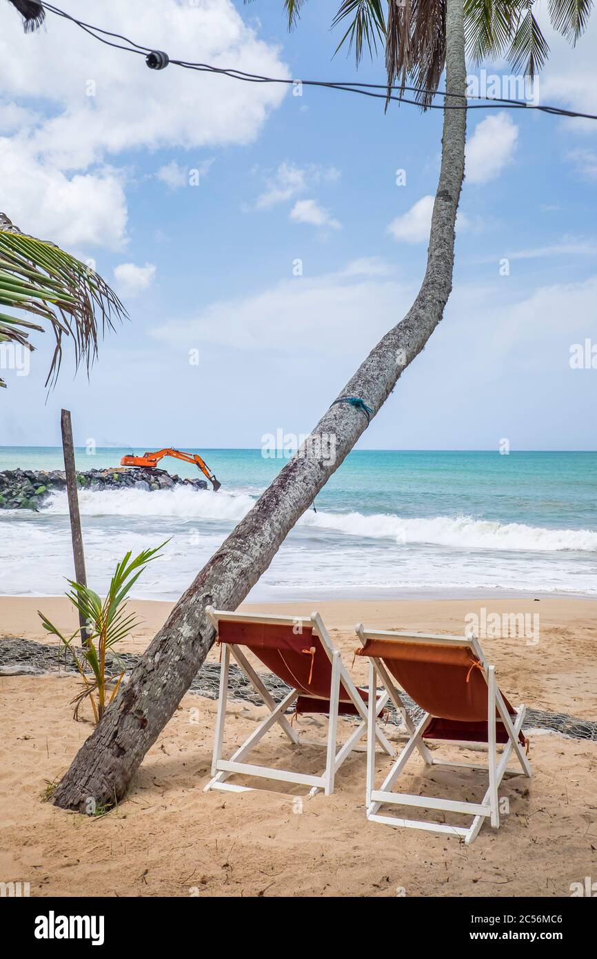 Beach chairs stand on the beach facing the sea with excavators on a ...