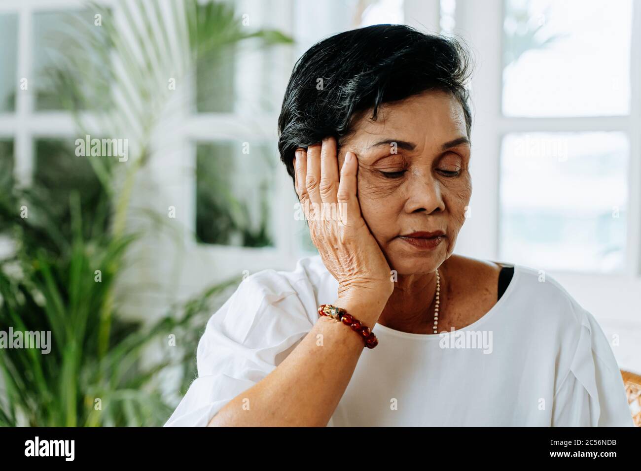 Stressed senior Asian female leaning on hand and pondering about ...
