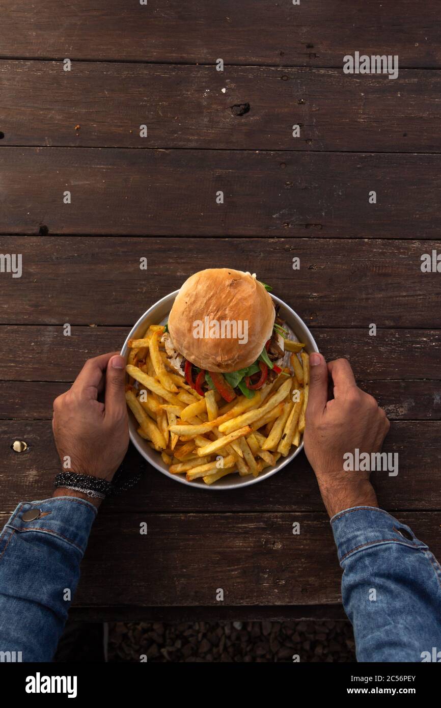 Male hands holding the white bowl full of French fries and a burger ...